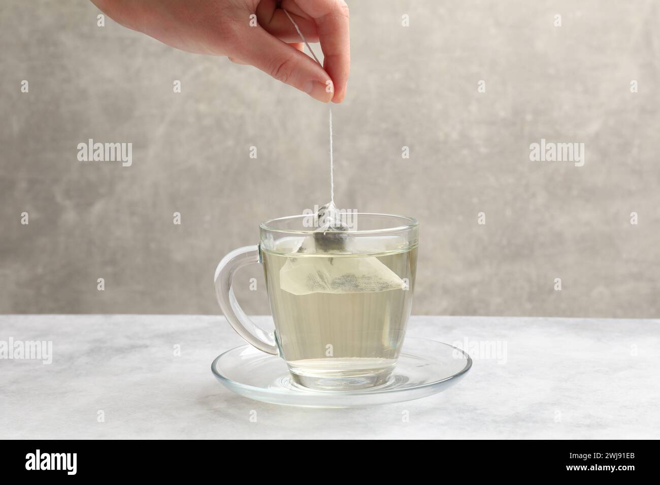 Tea brewing. Woman putting tea bag into cup at light table, closeup ...