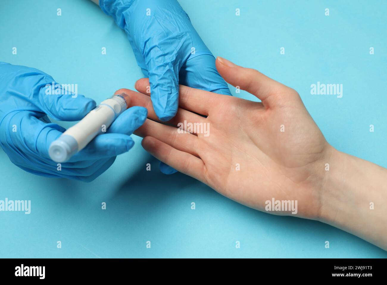 Diabetes. glucose testing. Doctor using lancet pen on light blue ...