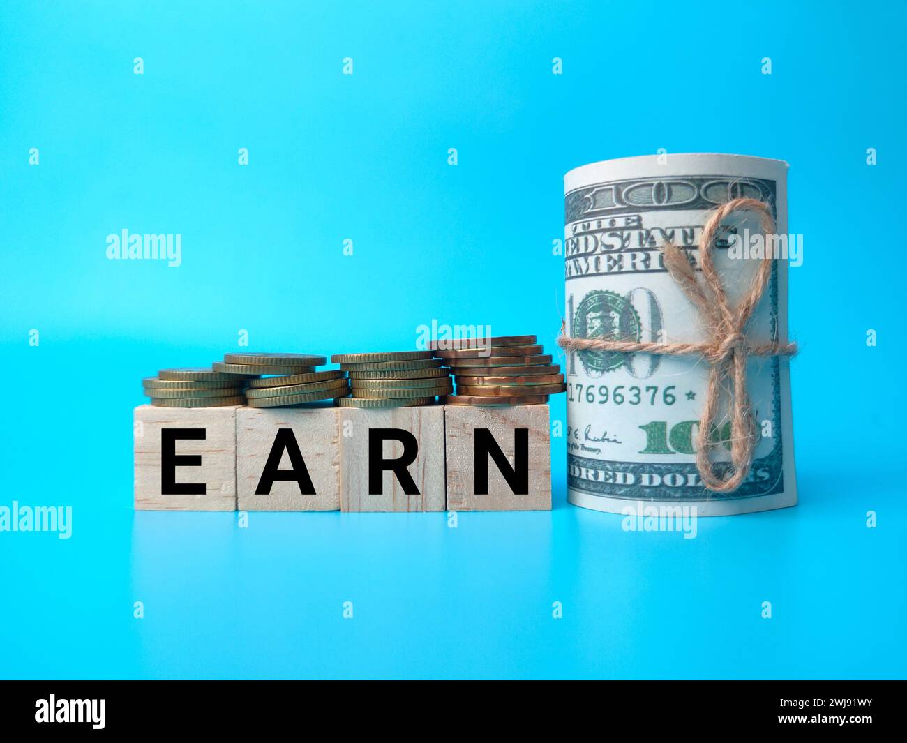 Wooden block,coins and banknotes with text EARN on a blue background ...
