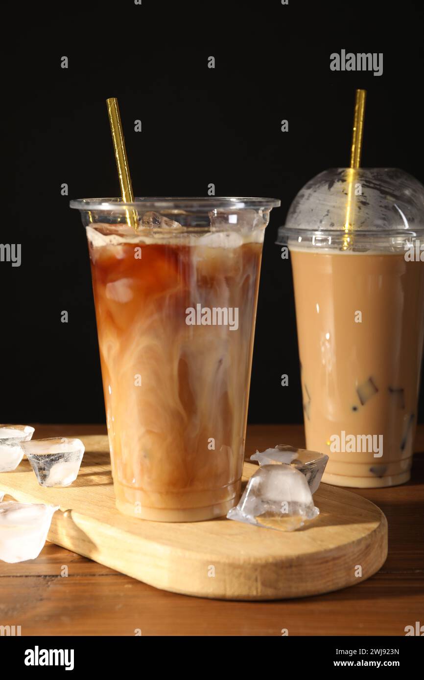 Refreshing iced coffee with milk in takeaway cups on wooden table ...