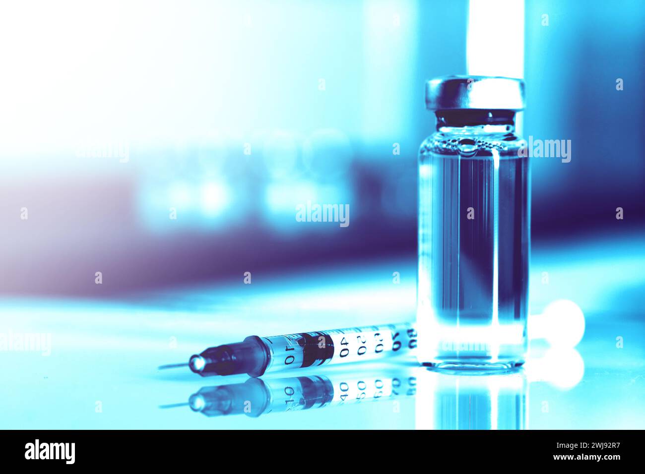 Syringe and glass vial with medication on mirror surface, toned in ...