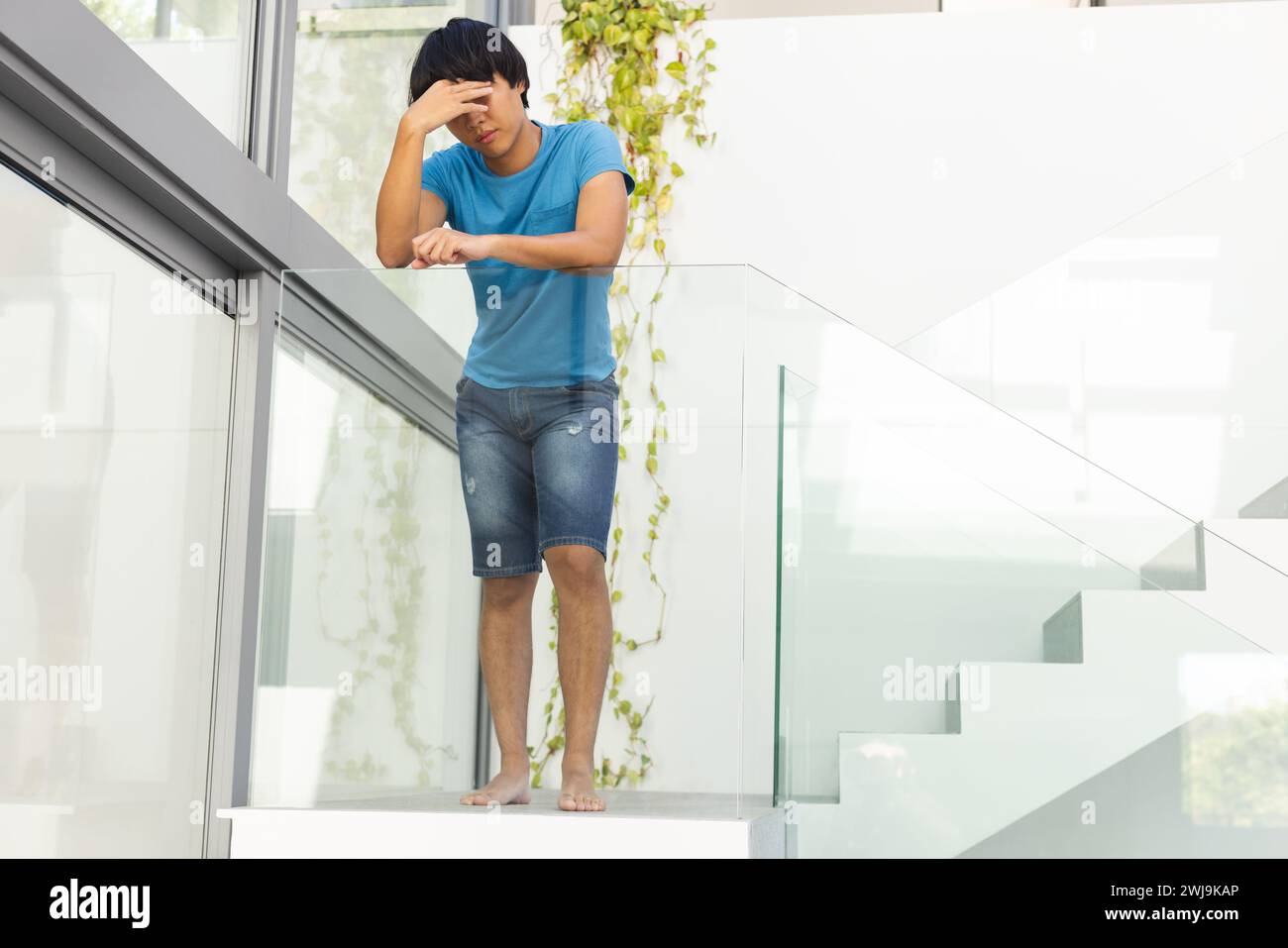 Teenage Asian boy stands on modern staircase at home, looking stressed ...