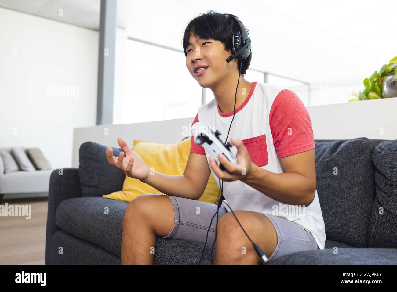 Teenage Asian boy enjoys gaming at home, with copy space. He's engaged ...