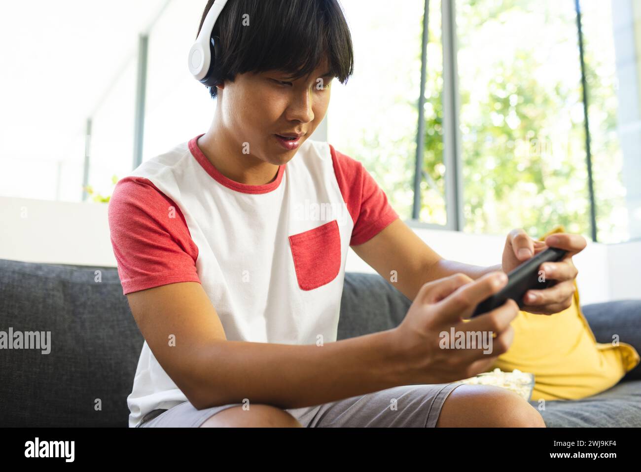 Teenage Asian boy enjoys gaming at home, focused and wearing headphones ...