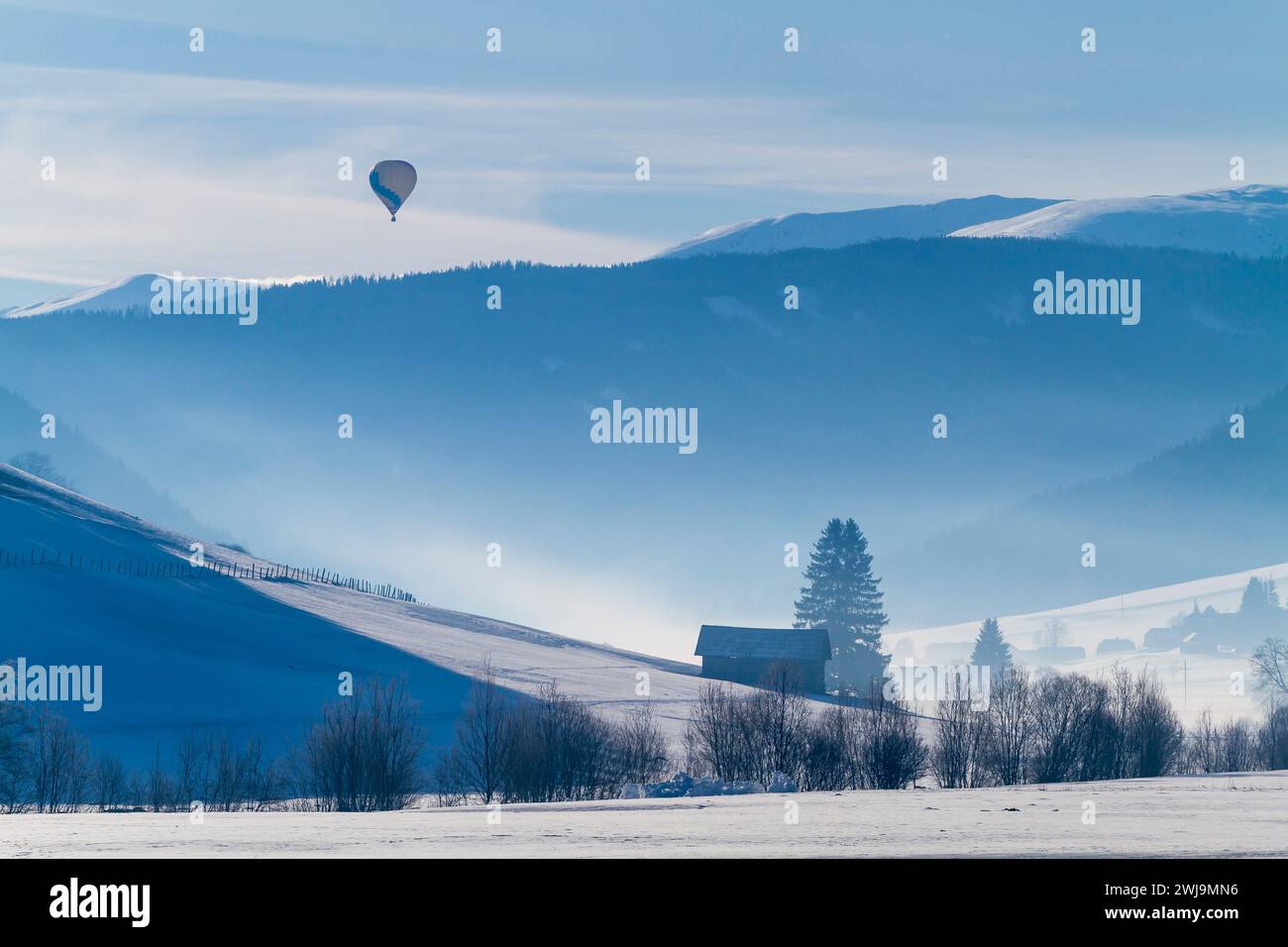 A hot air balloon floating over snow-covered mountains and valleys ...