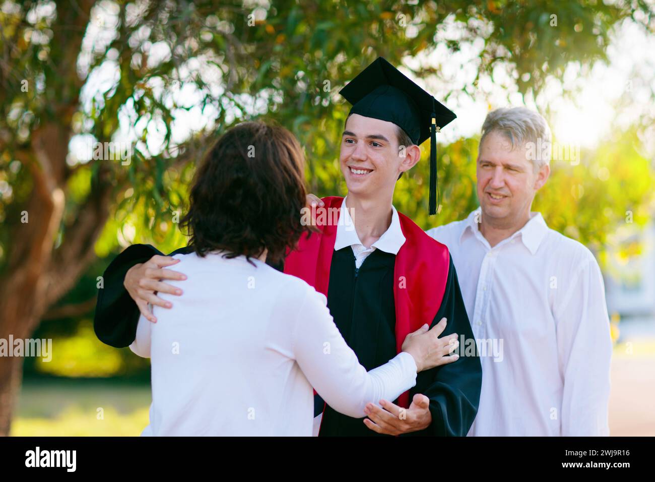 School or college graduation ceremony. Young man in gown and cap, with ...