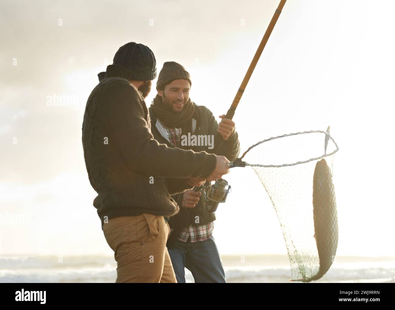 Fishing, men and net with fish at beach with rod, water and relax on ...