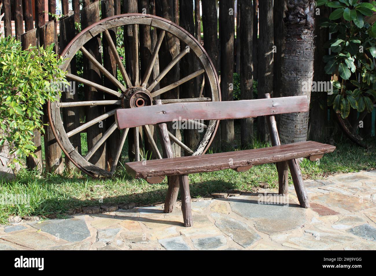 wooden cozy bench with a rustic old-fashioned wheel of wood with sunny ...