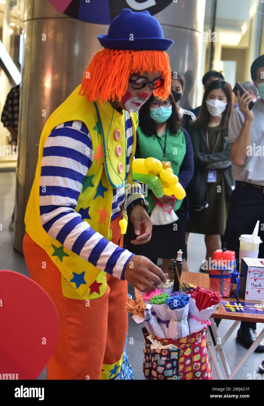 A person dressed in a clown costume makes shapes from inflated balloons ...