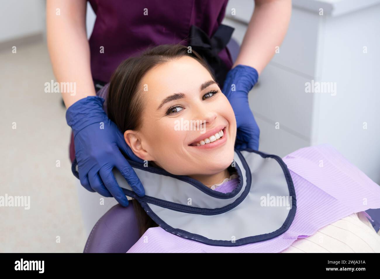 Dentist assistant wears shield for neck protection to patient before x ...