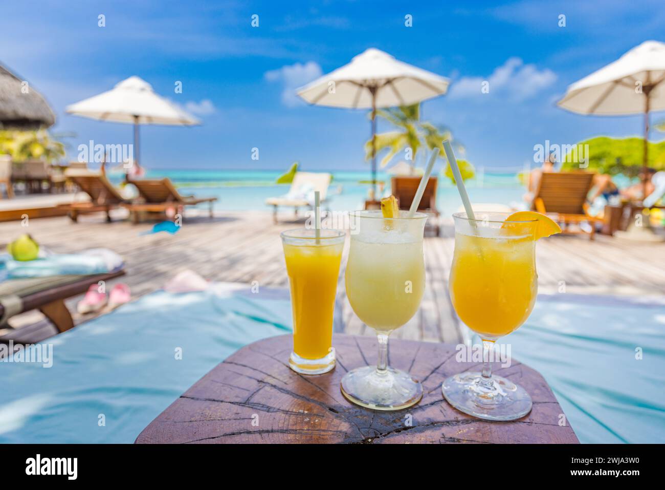 Colorful cocktails on luxury beach resort. Blurred poolside chairs beds ...