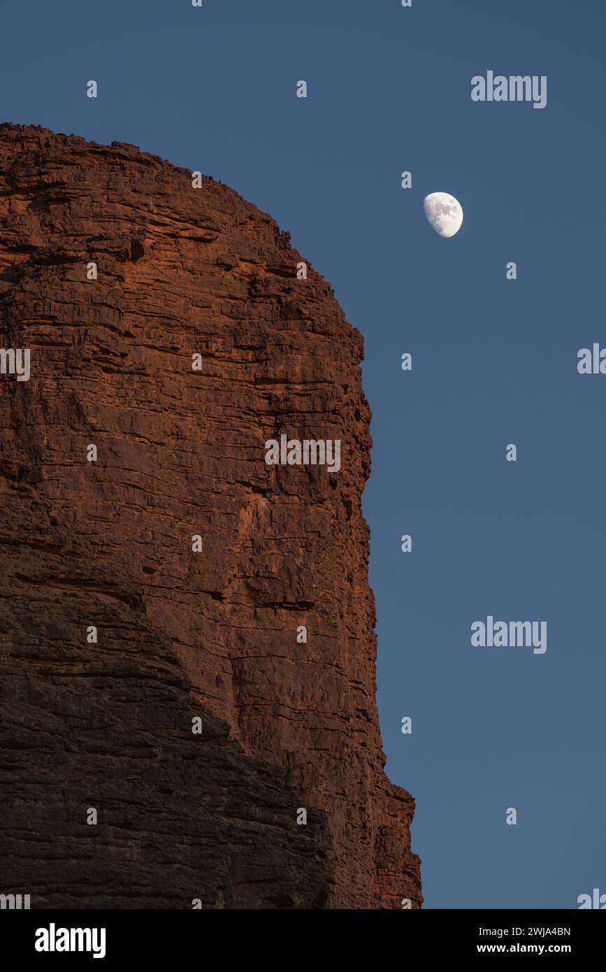 A serene view of the waxing gibbous moon beside a towering desert cliff ...