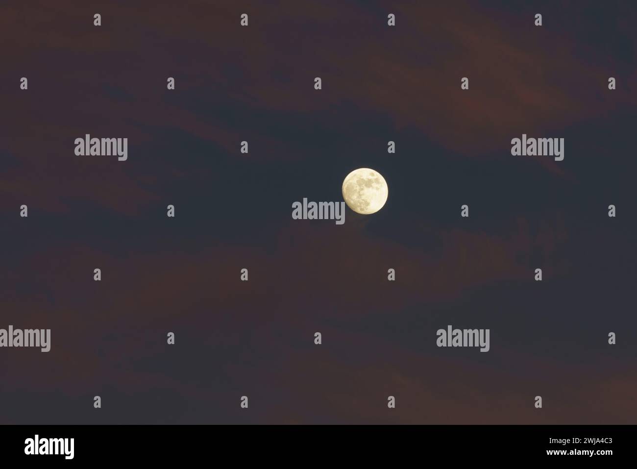 The full moon stands out against the twilight hues of the sky, casting ...