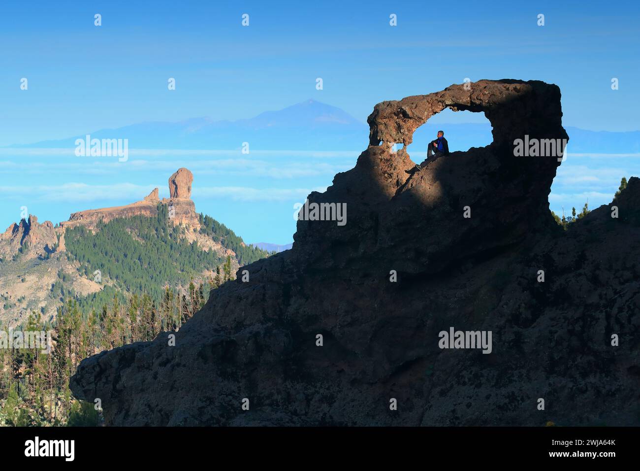A lone hiker is framed by a large natural stone arch overlooking a ...