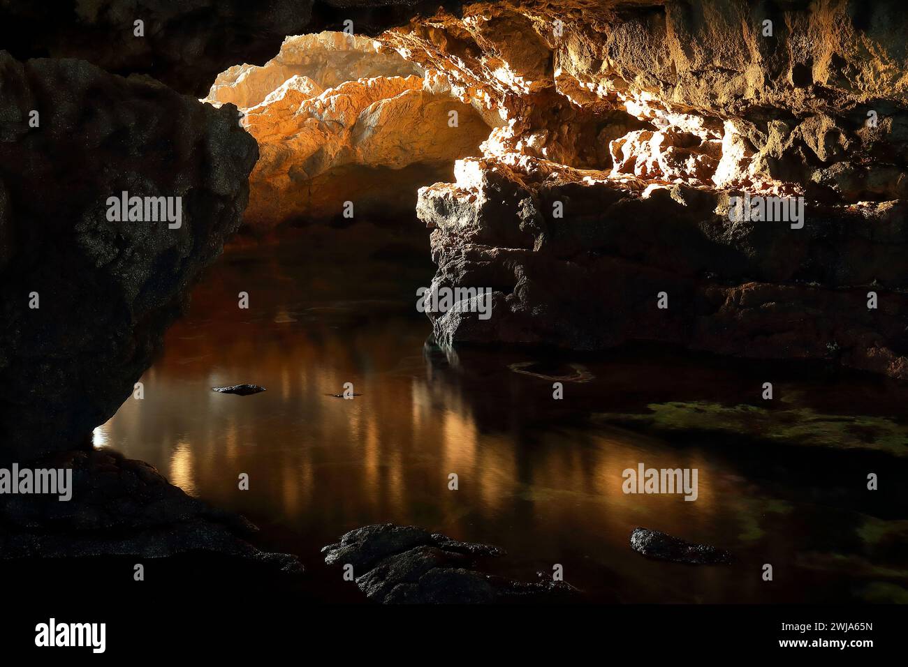 Warm light filters into a tranquil cave pool, highlighting the textured ...