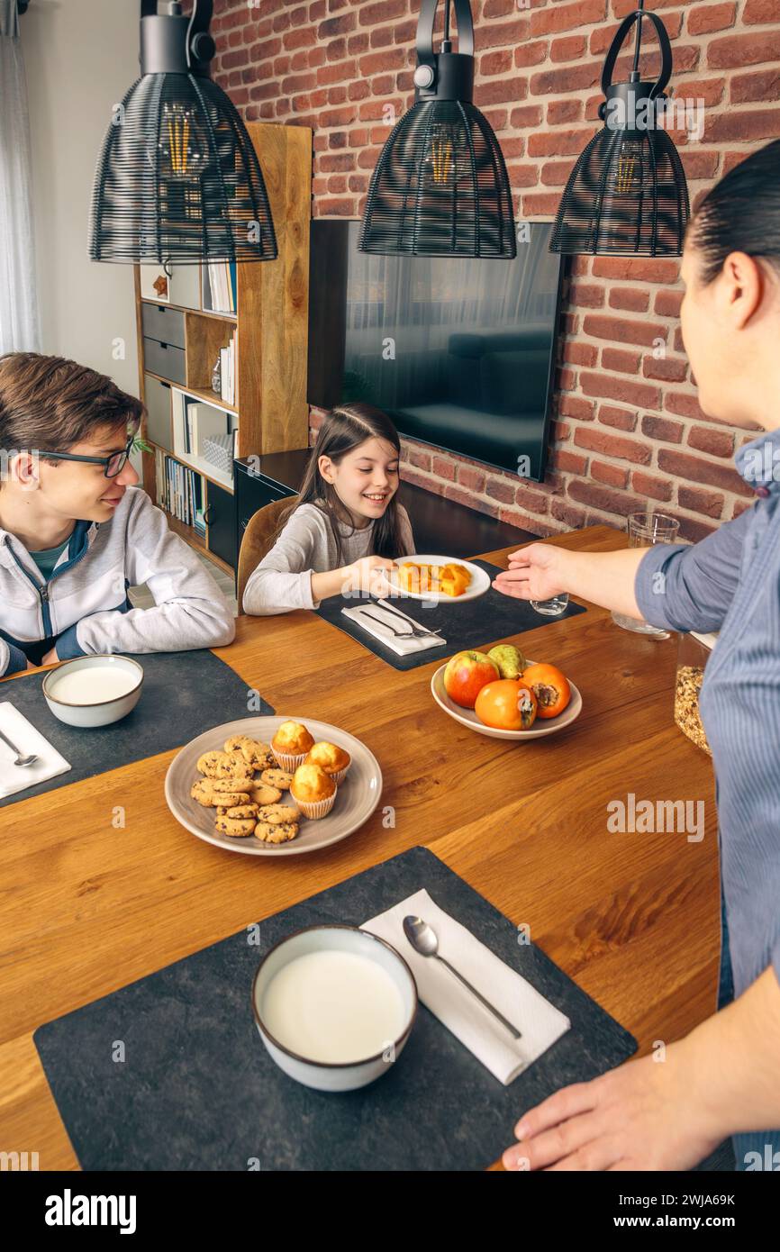 A parent serves sliced fruit to smiling children at a family breakfast ...