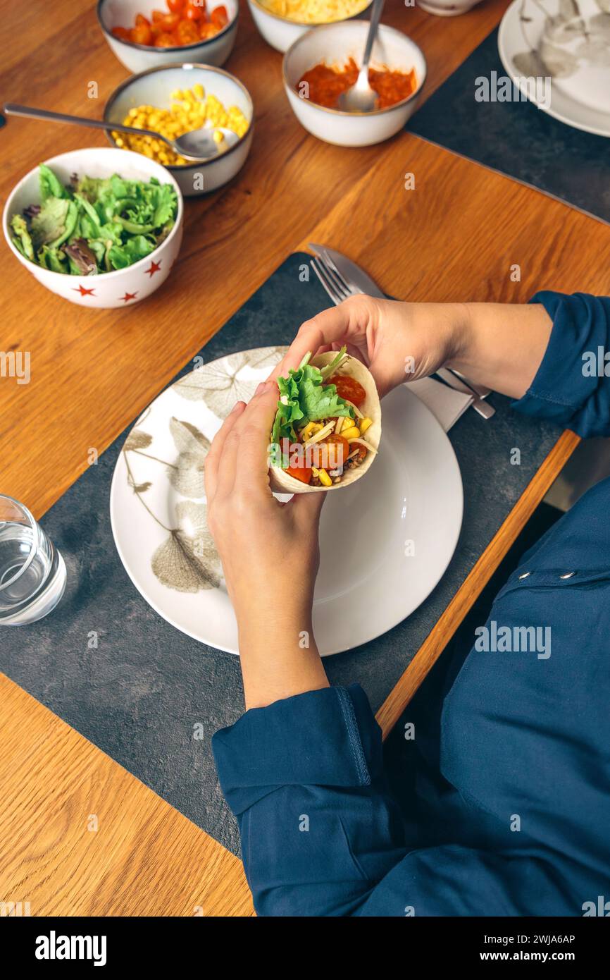Anonymous hands carefully hold a filled taco over a plate, with bowls ...