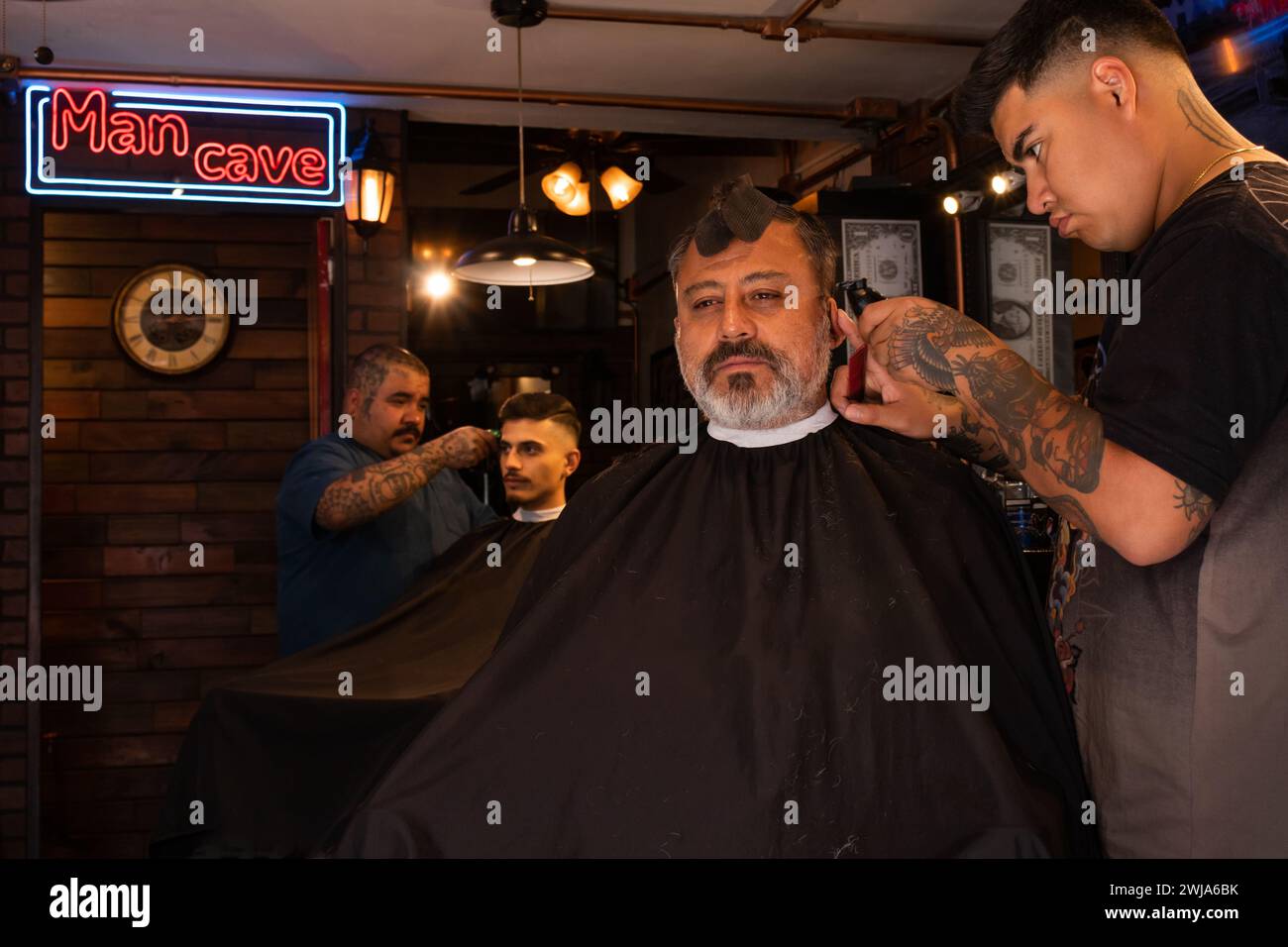 Side view of serious tattooed barber in black t shirt trimming hair of ...