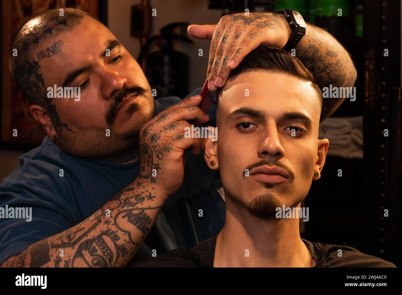 Serious barber with tattooed arm cutting hair of stylish guy with ...