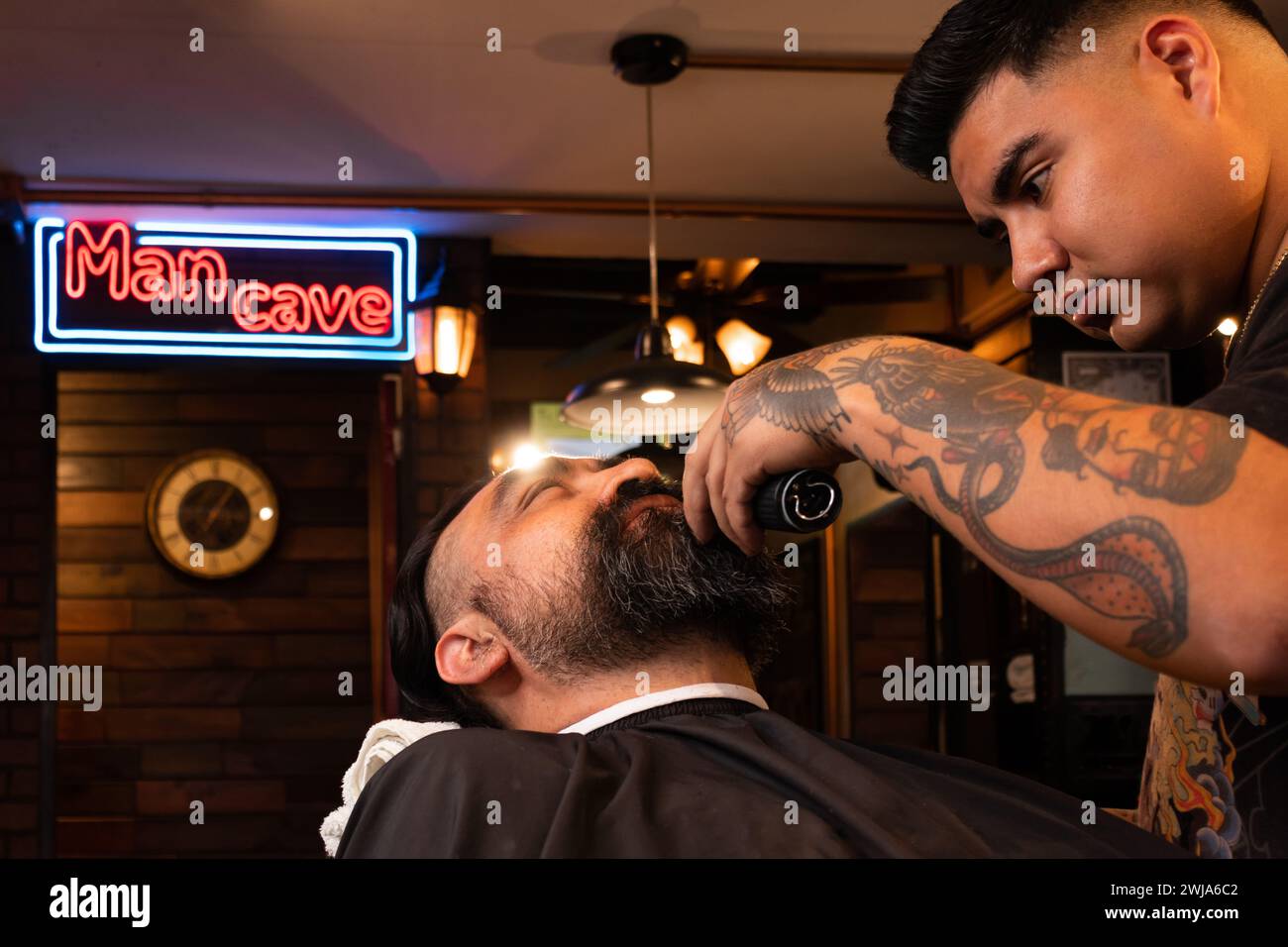 Barber trimming beard of customer in barber cape relaxing with towel ...