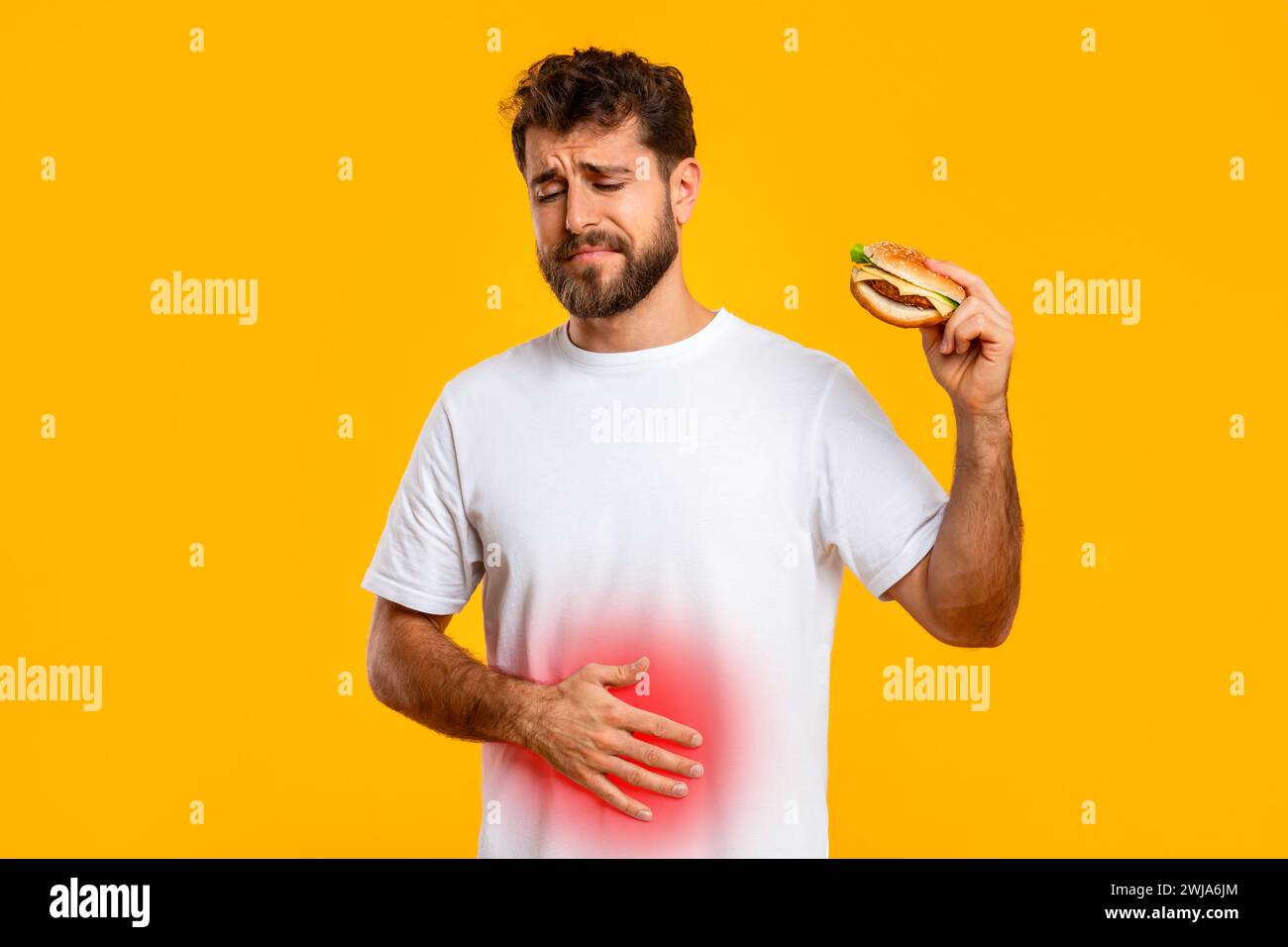 guy holding cheeseburger touching stomach on yellow studio background ...