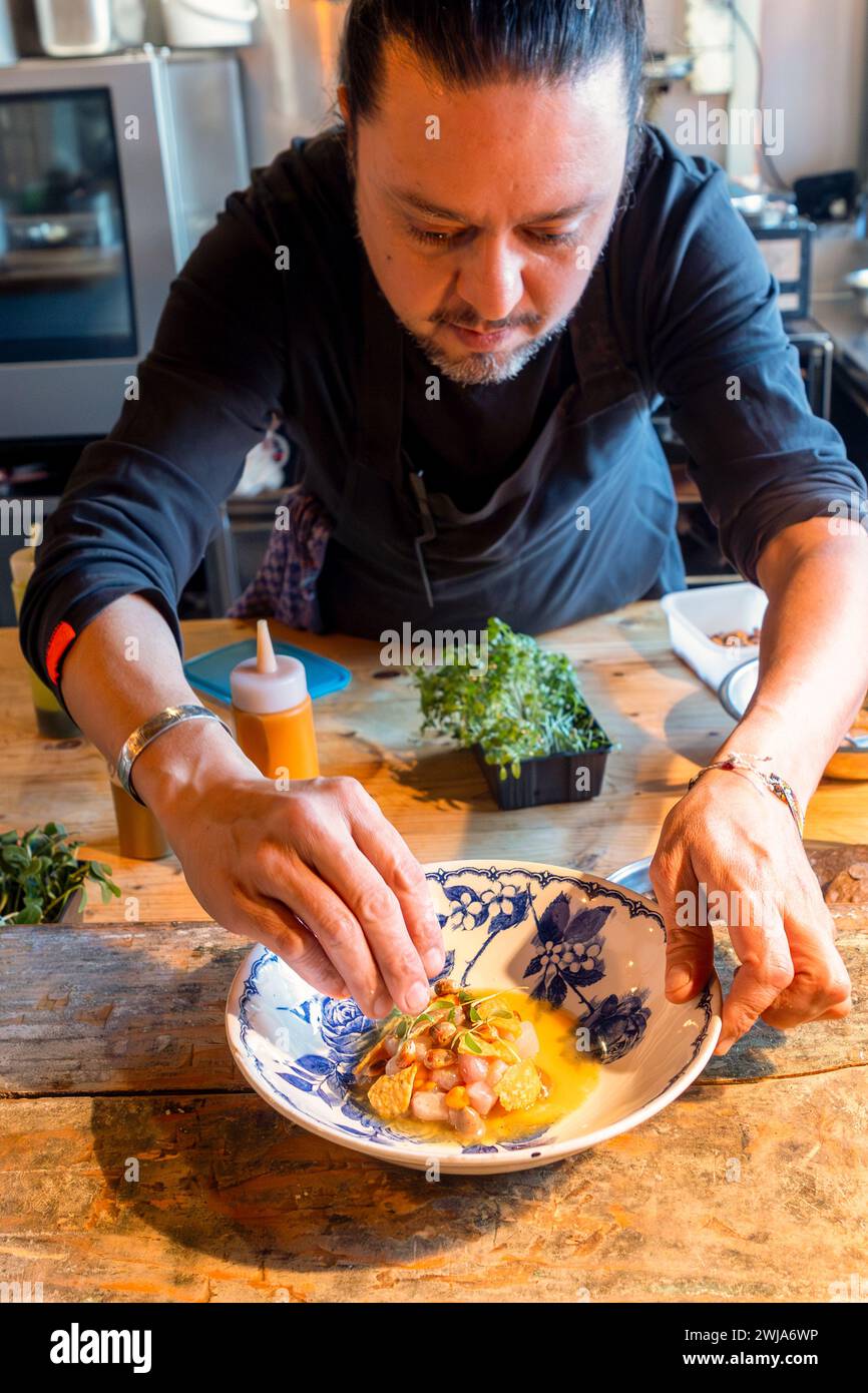 Concentrated mature chef in black uniform and apron serving fish ...