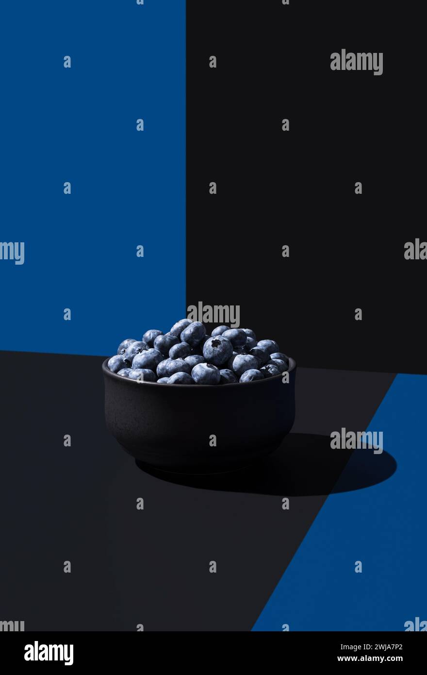 A minimalist composition featuring a black bowl of blueberries on a ...