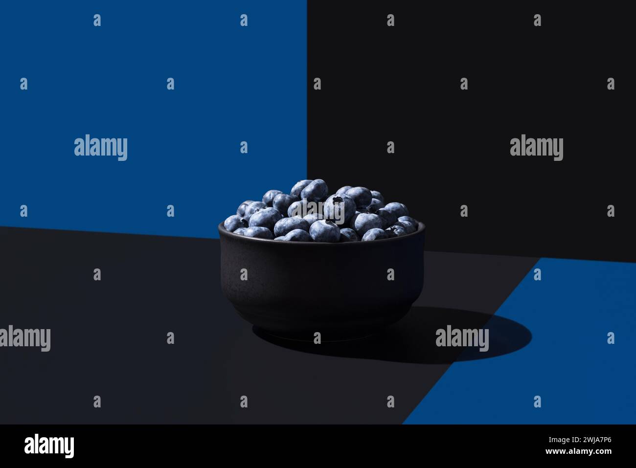 A minimalist composition featuring a black bowl of blueberries on a ...