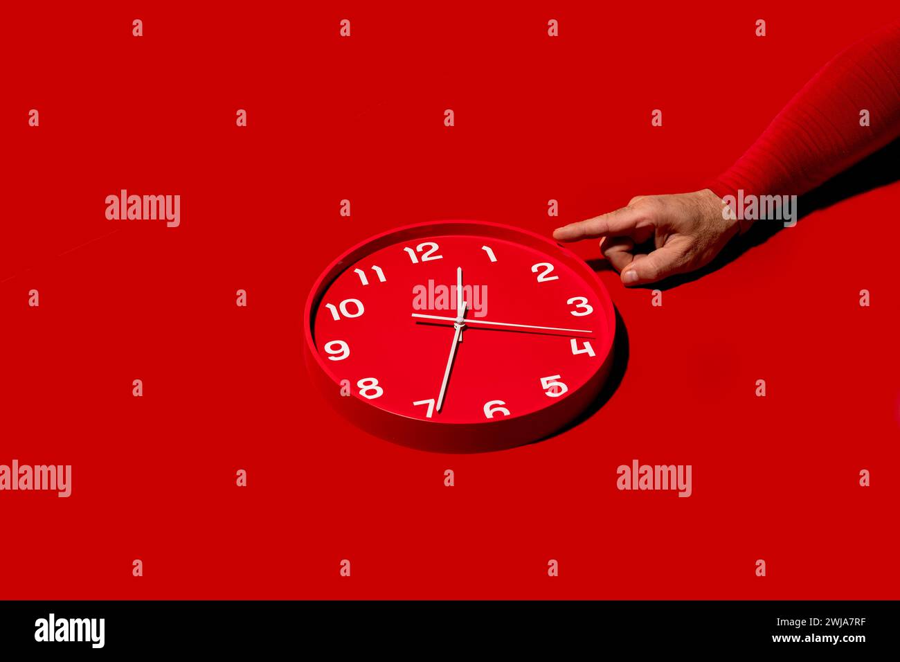 A person's hand pointing at a sleek red clock on a matching red ...