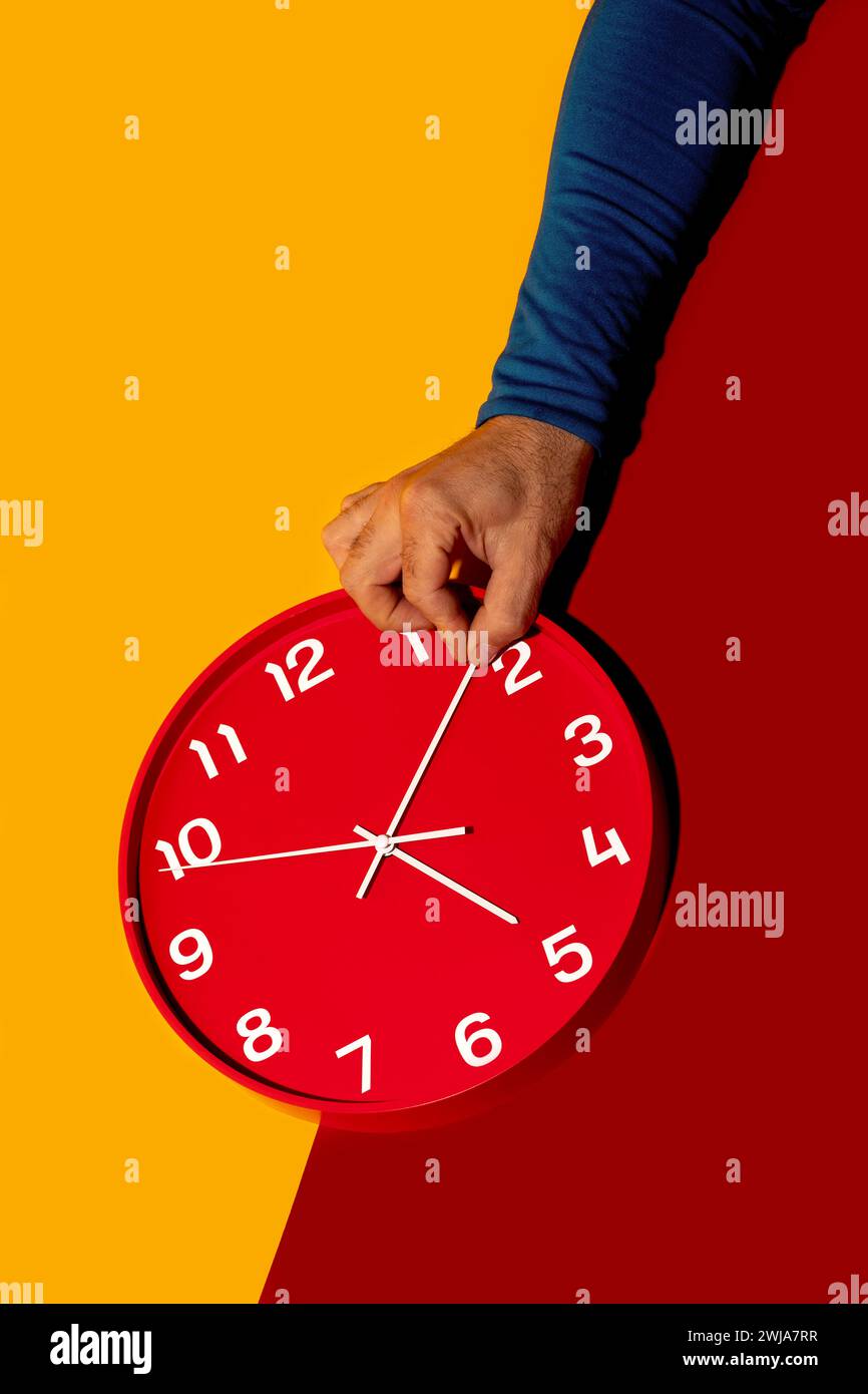 A person's hand sets the time on a vivid red clock contrasted against a ...