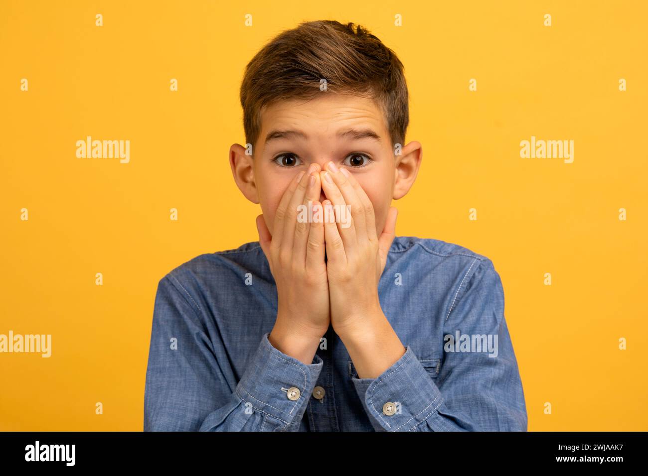 Teenage boy with shocked expression covering his mouth with both hands ...