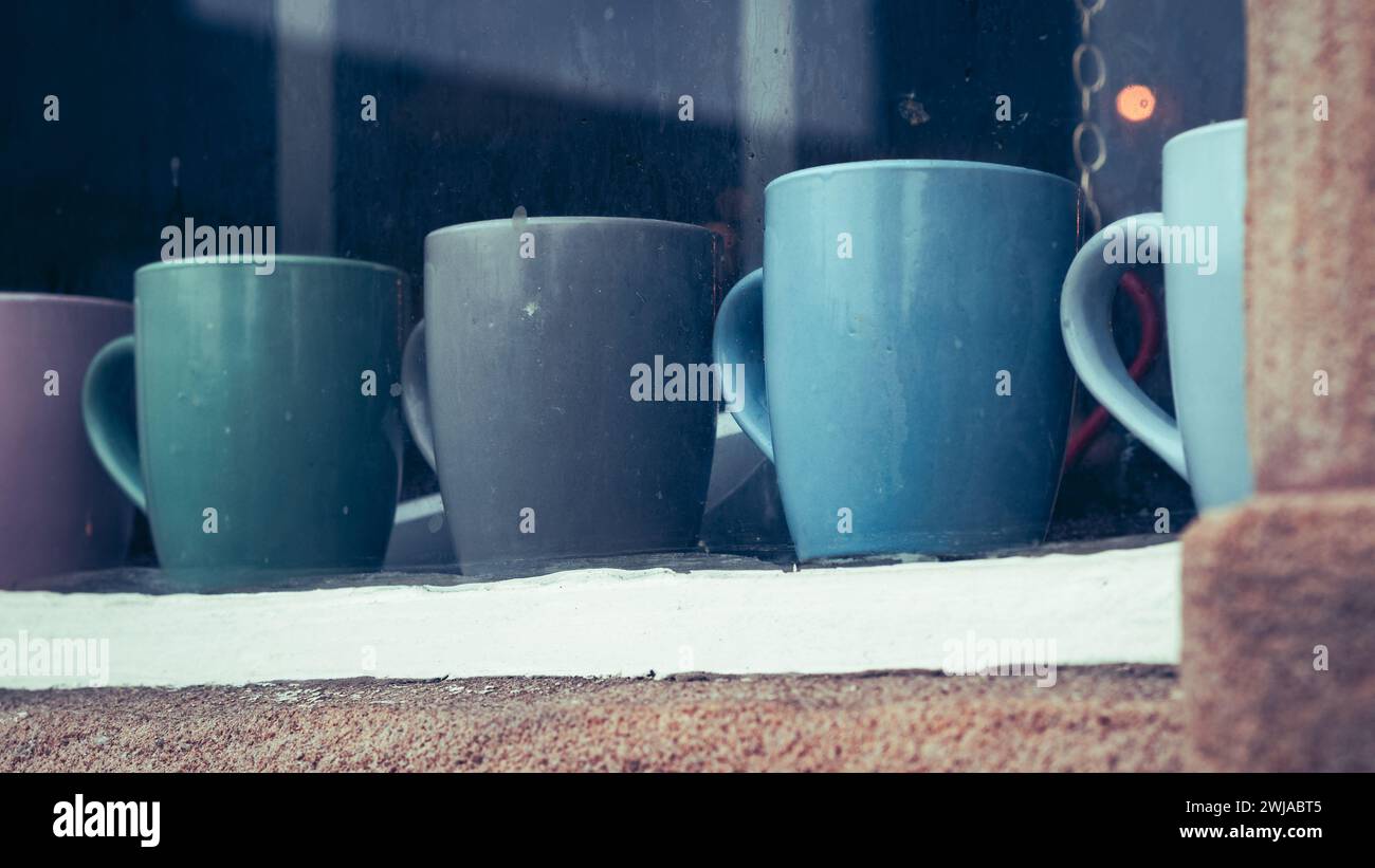 Row of coffee mugs on the coffee shop shelf behind the window looking ...