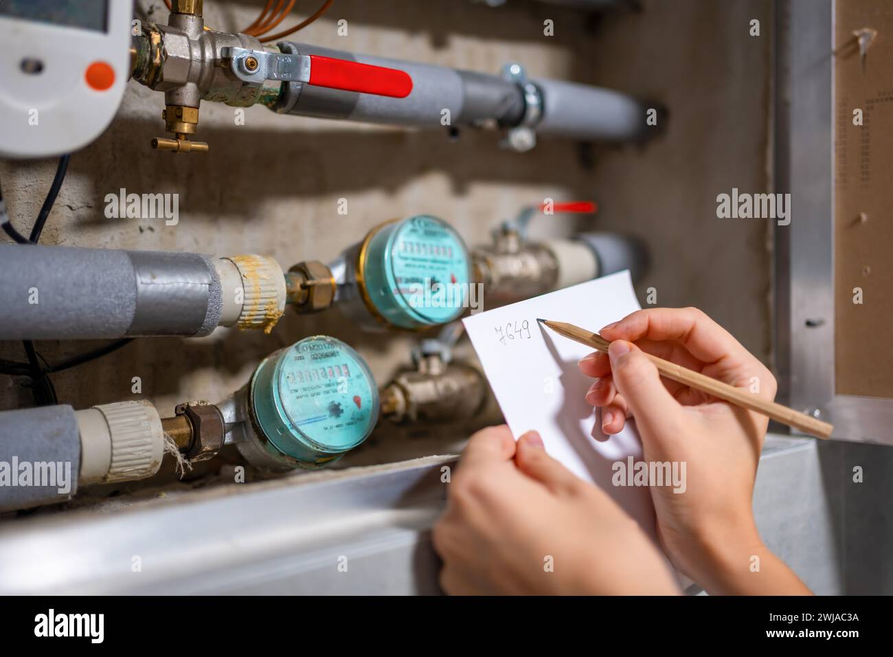 Woman recording meter readings, water meters of cold and hot water ...
