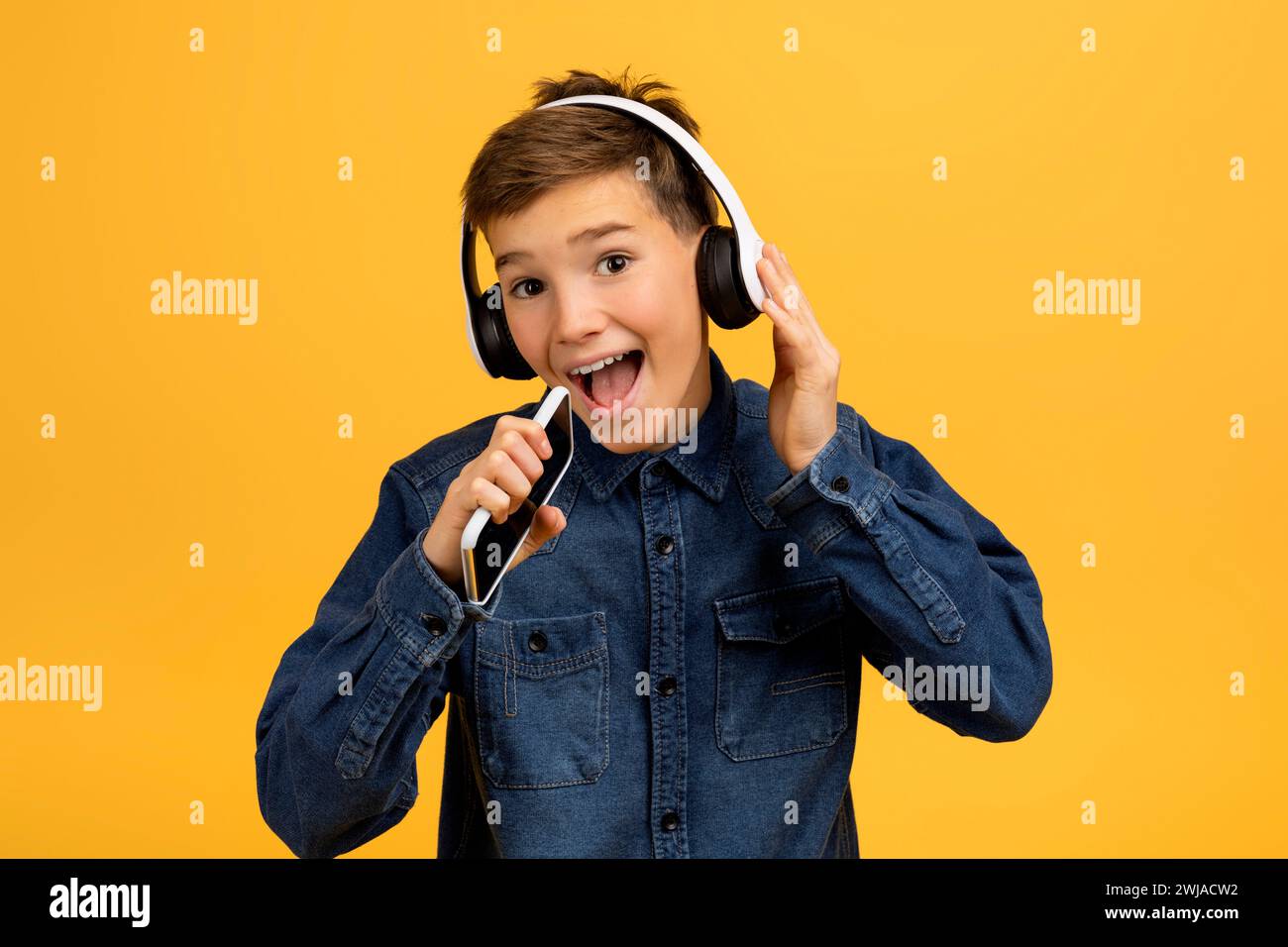 Positive male kid wearing wireless headphones singing while listening ...