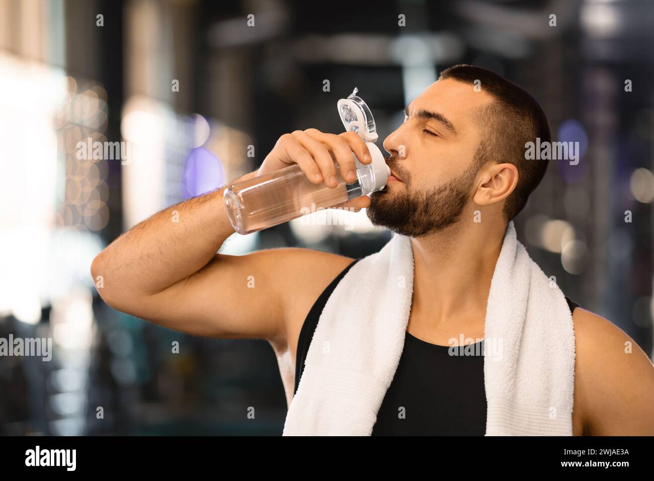 Sporty young man drinking water from bottle after training at modern ...