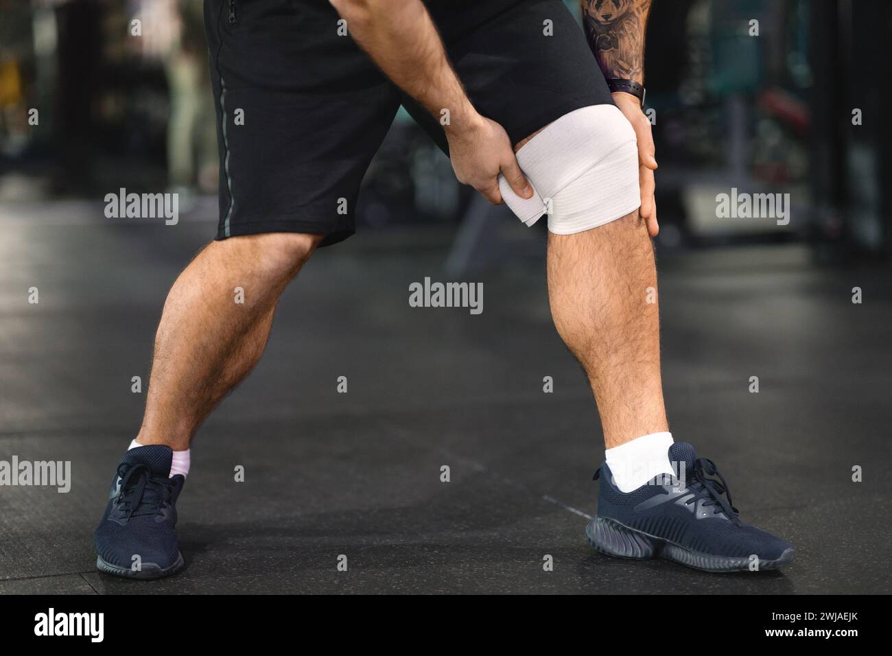 Sport Injury. Male athlete wrapping knee brace around his leg at gym ...