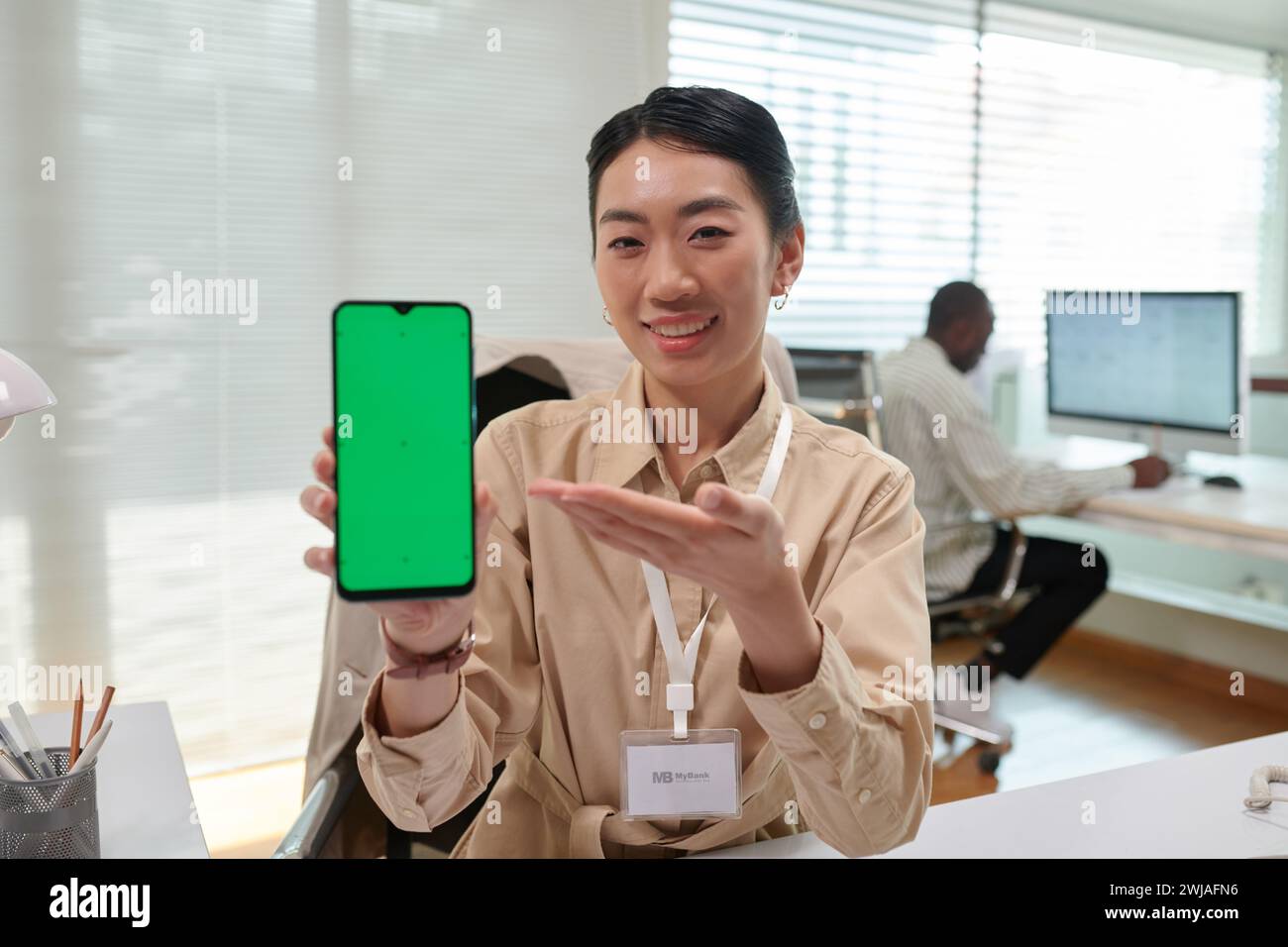 Portrait of smiling bank manager showing smartphone with green screen ...