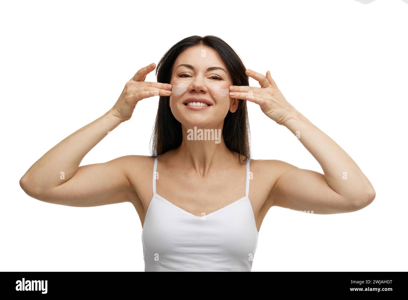 Portrait of happy brunette woman applies moisturized cosmetic product ...
