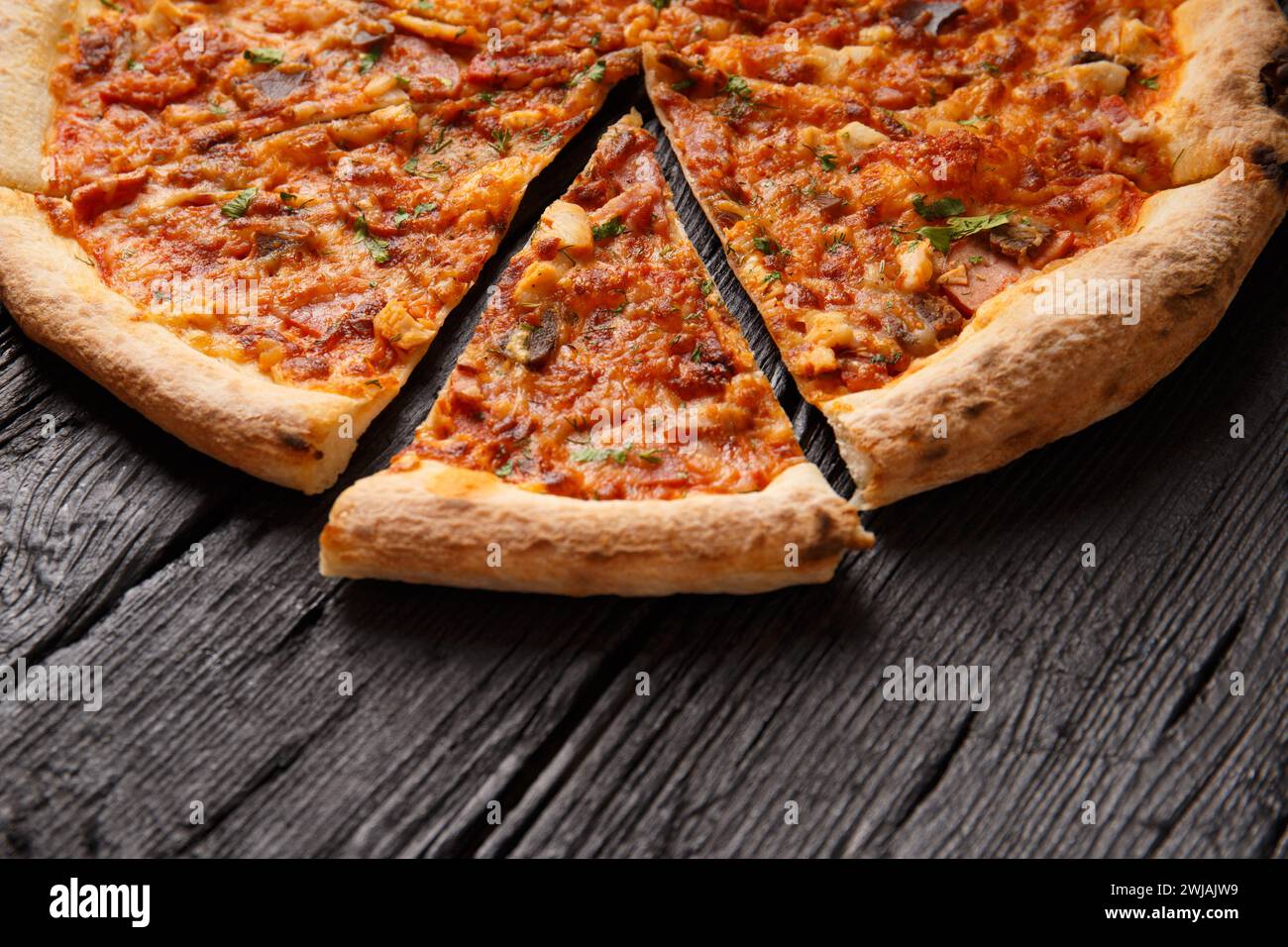 Pizza with different types of meat, cut into slices, one slice is ...