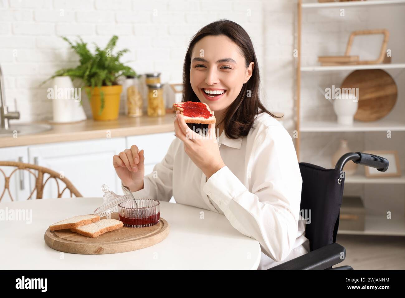 Happy young woman in wheelchair eating toast at home Stock Photo - Alamy