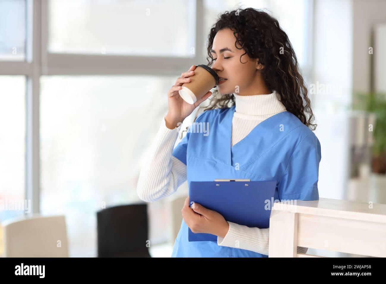 Female African-American medical intern with clipboard drinking coffee ...