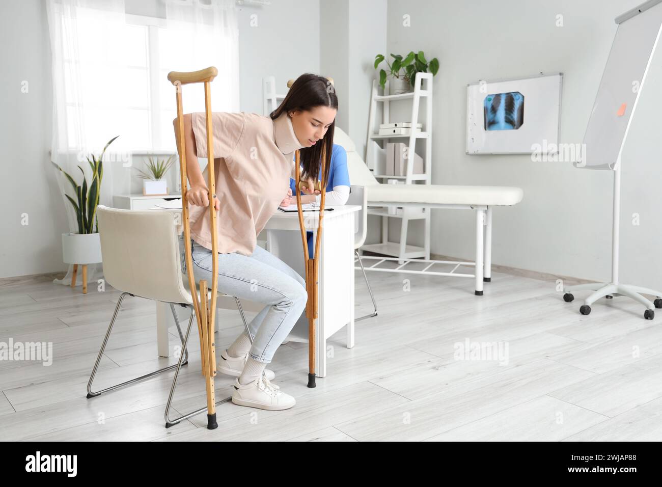 Injured young woman after accident with crutches standing up from chair ...