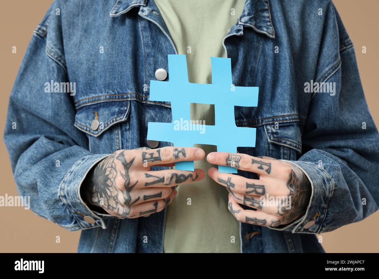 Cool tattooed young man with hashtag symbol on beige background ...