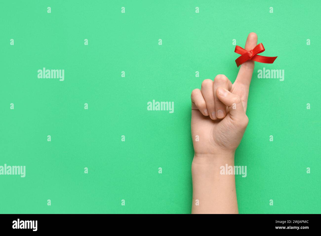 Female hand with red bow on index finger against green background ...