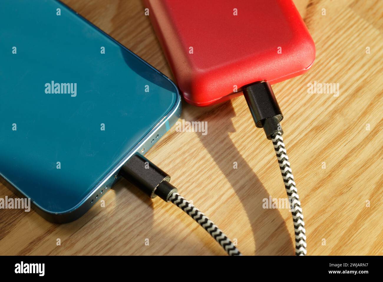 Back of red and blue two mobile phones connected to charging cables ...