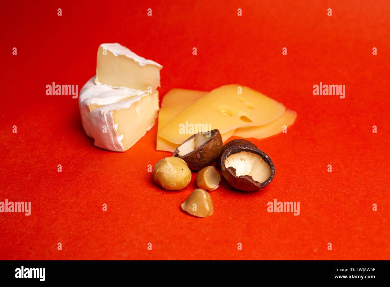 An assortment of hard and soft cheeses and macadamia nuts on a red ...
