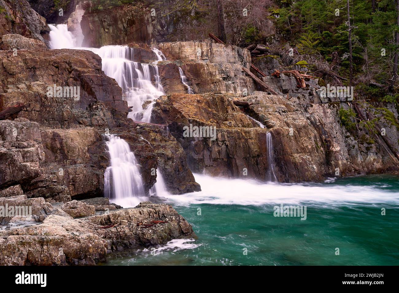 A waterfall rushing down a colorful cliff into the aqua waters below at ...