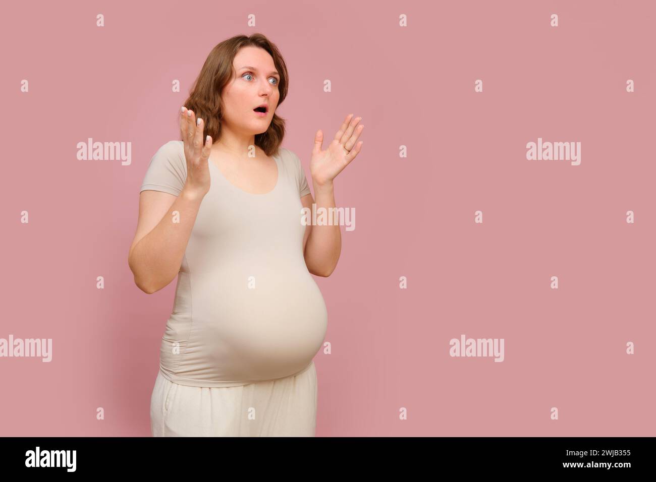 A scared pregnant woman on a pink studio background. Pregnancy in a ...