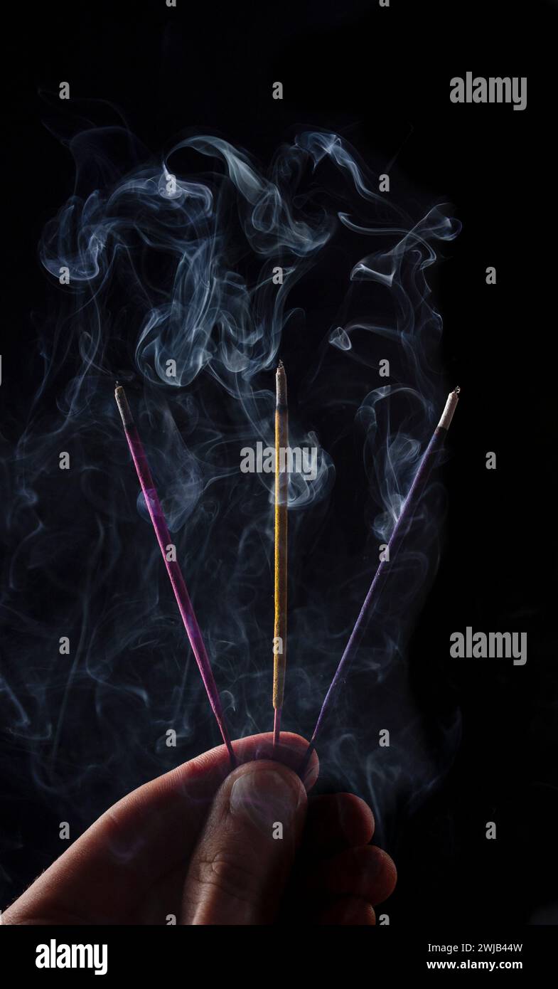 Three multi-colored incense sticks in a man's hand. Sticks are smoking ...