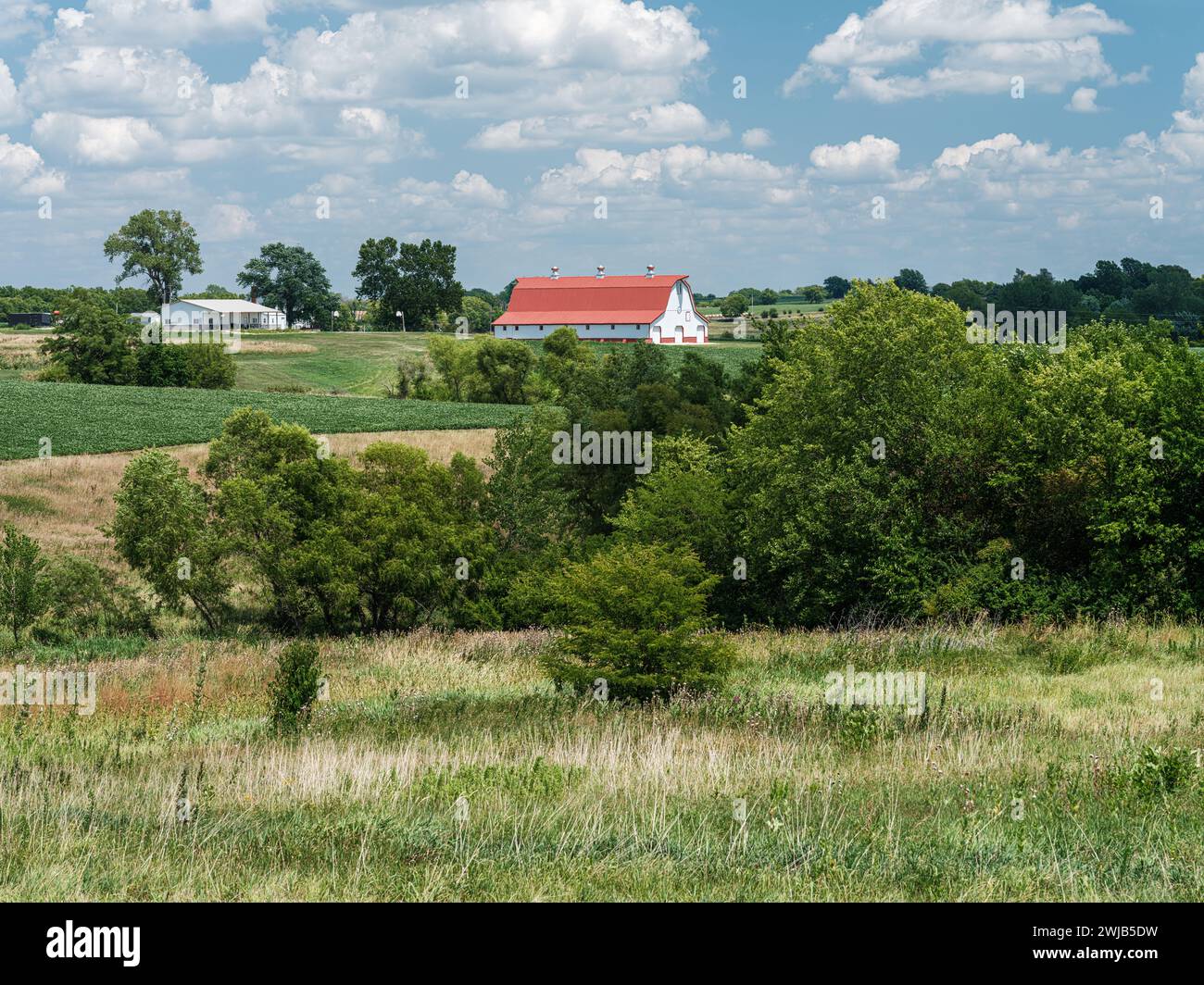 A beautiful red-roof barn sits idyllically shaped by a blue sky and ...